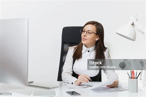 아름 다운 미소 브라운 헤어 비즈니스 여자 양복과 안경 책상에 앉아 현대 모니터 빛 사무실에서 문서를 컴퓨터에서 작업 보고