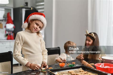 엄마가 아들과 놀고 있는 동안 진저브레드 쿠키를 색칠하는 카메라를 보고 있는 귀여운 소녀 2 3 살에 대한 스톡 사진 및 기타 이미지 2 3 살 25 29세 3 명