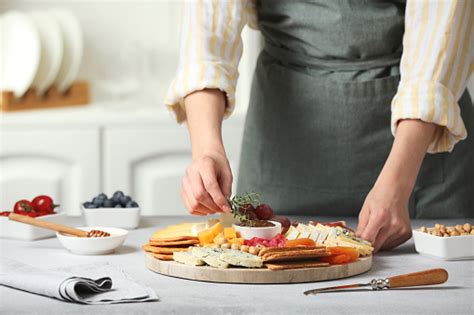 회색 질감의 실내 테이블에서 백리향과 함께 다양한 종류의 치즈와 다른 스낵을 곁들인 전채 접시를 제공하는 여성 근접 촬영 개체 그룹에 대한 스톡 사진 및 기타 이미지