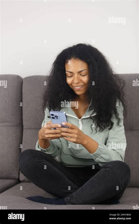 Happy Black Woman Sitting On Couch And Using Smart Phone App Cheerful