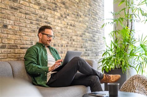 Handsome Confident Developer Working On Software Over Laptop While Sitting On Sofa In Modern