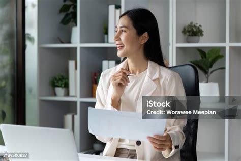 노트북과 문서를 들고 미소를 지으며 성공적인 비즈니스 성장을 위한 전략을 계획하는 현대적인 사무실 환경에서 자신감 넘치는 사업가 개발에 대한 스톡 사진 및 기타 이미지