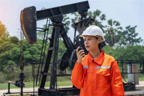 엔지니어가 워키토키를 사용하여 밝은 푸른 하늘을 배경으로 펌프 잭과 석유 굴착 장치를 검사하고 있습니다 작업 구역에서 보호복을 착용하고 작업하는 엔지니어 35 39세에 대한