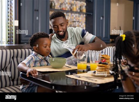 African american father pouring milk in bowl for son while having ...