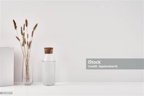 스파이크렛이 있는 투명한 화병과 흰색 배경에 코르크 스토퍼가 있는 물 한 병 미니멀리즘 내부 장식의 에코 소재 공간을 복사하고