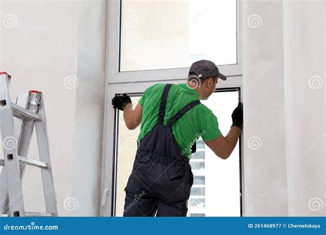 Worker In Uniform Installing Double Glazing Window Indoors Back View