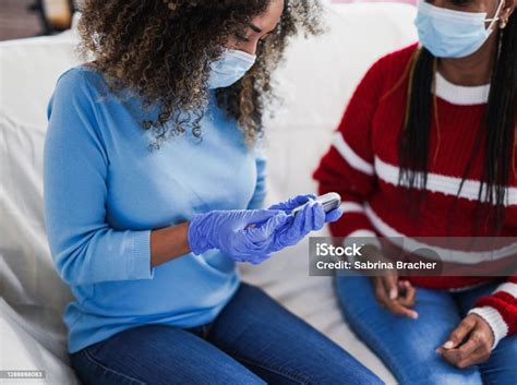 외과 장갑과 얼굴 마스크를 착용하는 동안 코로나 바이러스 잠금에 대한 수석 아프리카 환자의 집에서 당뇨병 설탕 검사를하고 간호사 2명에 대한 스톡 사진 및 기타 이미지