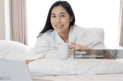 침대에 노트북에서 작업 목욕 가운에 행복 아름다운 아시아 여성 여자는 침실에서 커피 한 잔과 함께 침대에 누워 침대에 어린