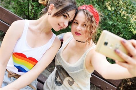 Dos amigas lesbianas se relevan en teléfonos con cámara o toman autofotos y sonríen Foto Premium
