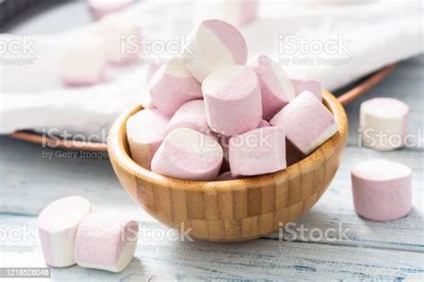 분홍색과 흰색 마시멜로로 가득 찬 나무 그릇을 닫고 흰색 테이블 천 어두운 쟁반 및 흰색 나무 테이블에 흩어져 있습니다 0명에