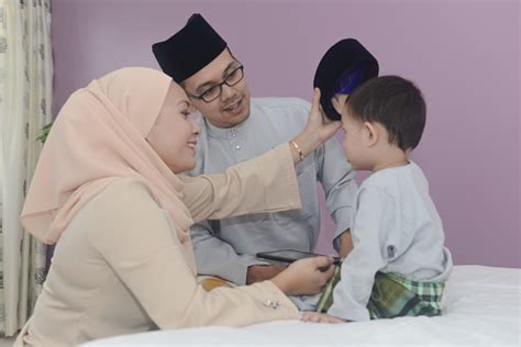 말레이시아 부모가 이드ulfitr 축 하 동안 집에서 전통적인 머리 장식을 착용 하는 자신의 어린 소년을 돕는 3 명에 대한