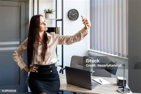 Pc 노트북으로 테이블에 기대어 셔츠와 치마를 입은 젊은 비서 직원 비즈니스 여성은 사무실에서 휴대 전화로 셀카 촬영을합니다 셀카에 대한 스톡 사진 및 기타 이미지 Istock