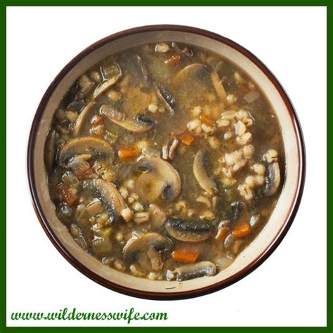 A Bowl Of Barley Soup With Mushrooms And Carrots In It On A White