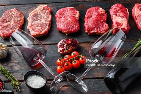 조미료와 레드 와인이 있는 다른 생 소고기 스테이크 세트와 오래된 목재 어두운 판자 옆 전망의 유리 0명에 대한 스톡 사진 및