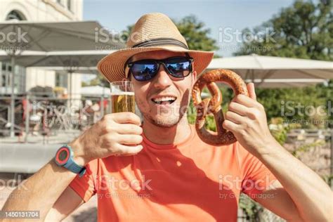 맥주 한 잔을 마시고 Biergarten 또는 야외 바에서 전통적인 독일 스낵 프레첼을 물고있는 행복한 관광객 35 39세에