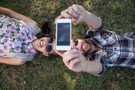 Premium Photo Young Couple Lying On Grass Taking Selfie