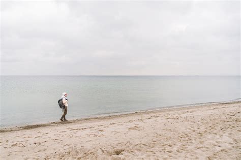 겨울에 발트 해 근처의 모래 해변에 검은 배낭을 가진 백인 남자 젊은 백인 여자 관광 한 사람 혼자 테마 여행 수평선을 내려다