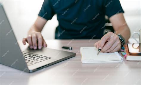Premium Photo Young Man Writing Down On Notebook And Using Laptop