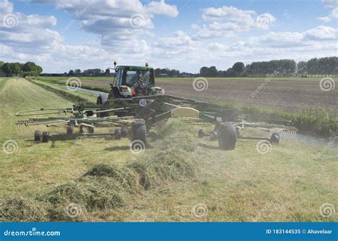 Tractor In Field With Grass Tedder During Hay Harvest In The
