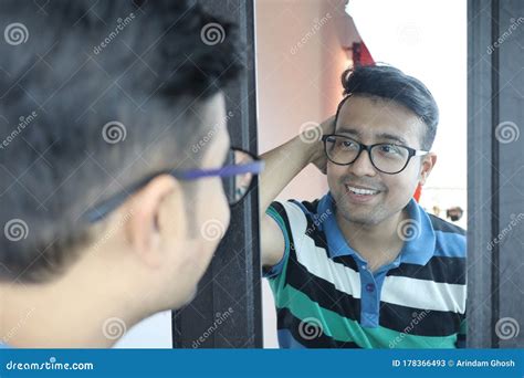 A Man With Eyeglass Looking At His Reflection In Mirror And Smiling At