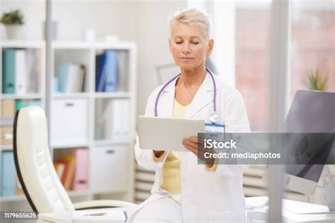 의료 웹 프로젝트를 보는 동안 테이블에 앉아 태블릿을 사용하여 짧은 머리와 심각한 바쁜 매력적인 성숙한 여자 간호사에 대한 스톡 사진 및 기타 이미지 Istock