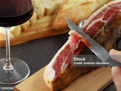칼을 든 남성 손은 원래 Jamon Serrano 햄을 조각으로 자르고 클로즈업 배경에 레드 와인과 빵이있는 세트 테이블에