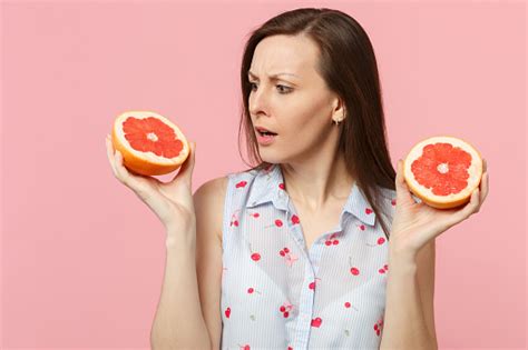 여름 옷에 젊은 여자를 의아해 스튜디오에서 분홍색 파스텔 벽 배경에 고립 된 신선한 익은 자 몽의 Halfs 손에 개최 합니다 사람들은 생생한 라이프 스타일 휴식 휴가