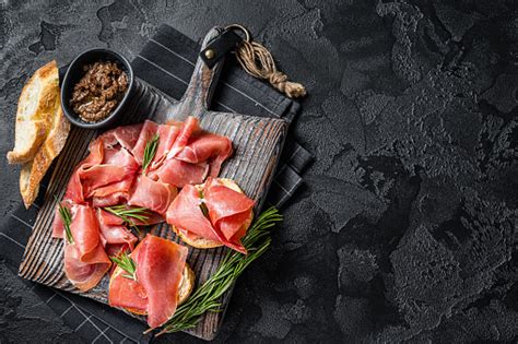 토마토와 자몬 세라노 햄의 경화 슬라이스 로즈마리와 나무 보드에 Prosciutto Crudo 파르마와 토스트 검은 색 배경 맨
