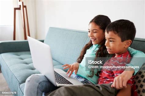 Kakak Dan Adik Duduk Di Sofa Di Rumah Bersenangsenang Bermain Di Laptop