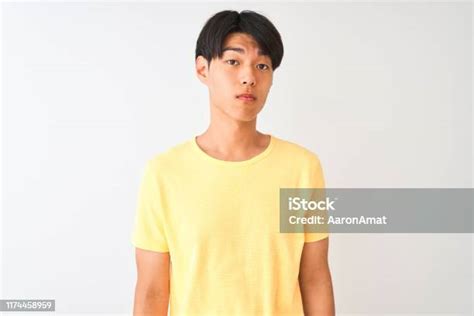 노란색 캐주얼 티셔츠를 입은 중국인 남성이 고립된 흰색 배경 위에 서 있는 모습이 얼굴에 진지한 표정을 짓고 있다 카메라를 보는