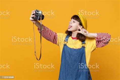 프랑스어 베 레모에서 재미 소녀 십 대는 복고풍 빈티지 사진 카메라에 Selfie 샷을 하 고 혀를 보여주는 노란색 배경에 고립