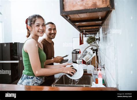 Young Asian Woman And Man Smiling While Washing Dishes Together Stock
