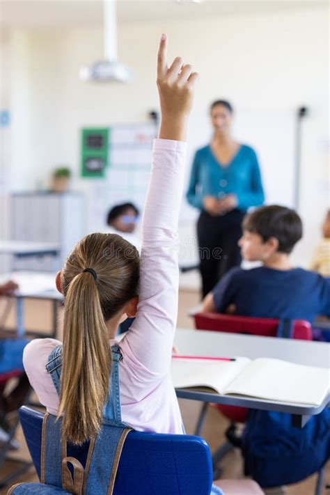 In School Girl Raising Hand To Ask Question In Classroom With Indian