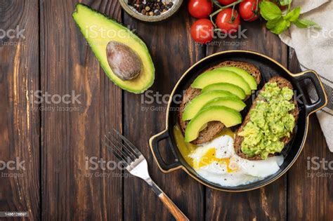 통밀 빵 토스트 얇게 썬 아보카도 수란이 소박한 테이블에 놓여 있습니다 건강한 아침 식사 아보카도와 계란 샌드위치 위에서 볼 수