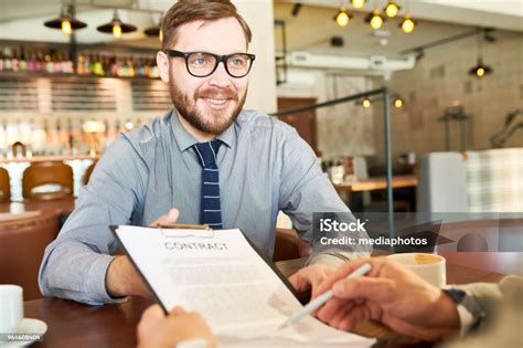 쾌활 한 자신감 잘생긴 남성 영업 관리자 새로운 사업 파트너와 계약을 체결 하 고 레스토랑에서 비공식 회의에서 계약을 보여주는