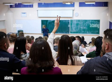 Rear View Of Female Student Sitting In The Class And Raising Hand Up To