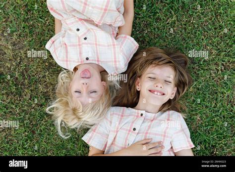 Cute Girl Sticking Out Tongue Lying By Happy Sister On Grass Stock