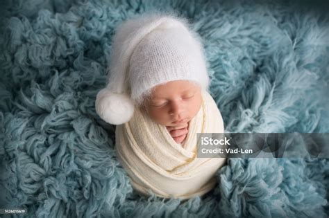 푸른 배경에 뜨개질 된 모직 흰 모자가있는 흰색 부드러운 누에 고치에서 삶의 첫날에 잠자는 신생아 소년 스튜디오 매크로 사진 신생아의 초상화 여성의 행복 1개월에 대한 스톡
