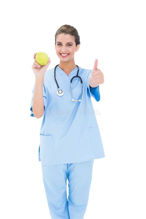 Cheering Brown Haired Nurse In Blue Scrubs Holding A Green Apple Stock