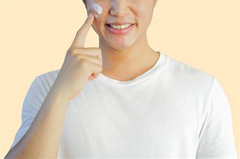 광고에 제품 개념에 대한 크림 배경에 고립 된 얼굴에 자외선 차단제를 적용젊은 아시아 남자를 닫습니다 남자에 대한 스톡 사진 및
