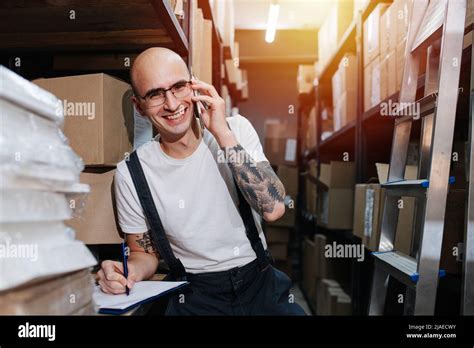 Social Smiling Male Warehouse Worker Talking On The Phone Writing On A