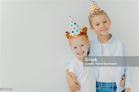 행복 한 작은 생강 주근깨 소녀와 어린 소년 포옹 하 고 기꺼이 미소 파티 모자를 착용 함께 좋은 시간을 즐길 수 흰색 배경