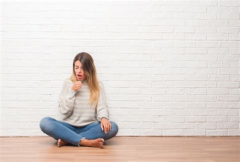 흰색 벽돌 벽 집에서 바닥에 앉아 젊은 성인 여자 기분이 불쾌 증상 감기 나 기관지염으로 기침 의료 개념입니다 천식에 대한 스톡
