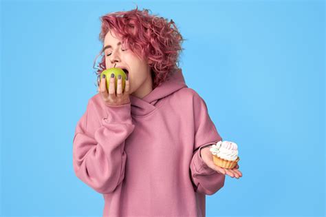 신선한 녹색 사과를 먹고 다른 손에 컵 케이크를 들고 핑크 곱슬 머리를 가진 소녀 마인드풀 이팅에 대한 스톡 사진 및 기타