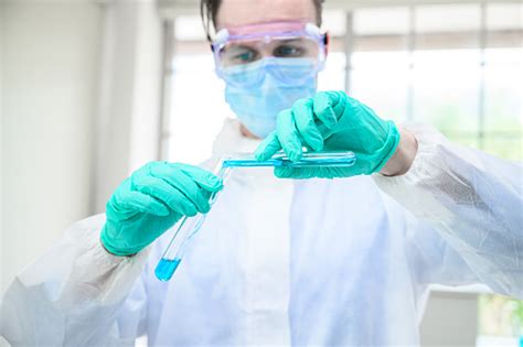 비커 나 튜브를 들고 샘플 액체와 보호 복을 입고 실험실에서 연구를위한 많은 실험실 장비와 함께 작업 하는 남성 과학자 Dna에