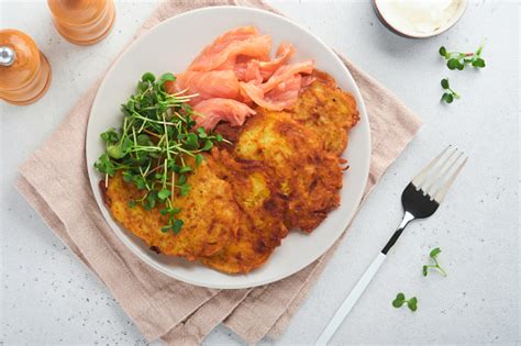 감자 팬케이크 흰색 테이블 배경에 소박한 접시에 크림 파 마이크로 그린 붉은 연어와 소스와 함께 집에서 만든 감자 팬케이크 또는