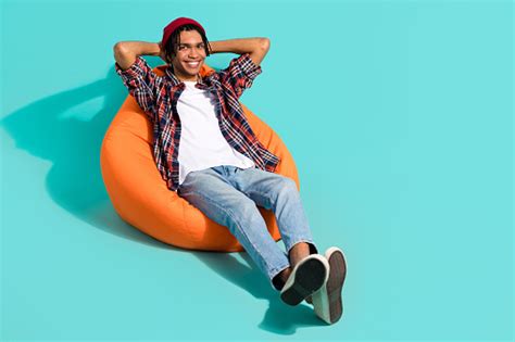 체크 무늬 셔츠를 입고 비니 모자를 쓰고 청록색 배경에 고립된 머리 뒤에 팔을 들고 있는 편안한 만족한 남자의 전체 길이 사진 18 19세에 대한 스톡 사진 및 기타 이미지