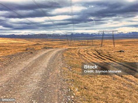 아이슬란드의 배경으로 눈이 덮인 산이 있는 번개와 고전압 전력선이 있는 극적인 하늘 아래 광야를 통과하는 자갈 길 계시록에 대한 스톡 사진 및 기타 이미지 Istock