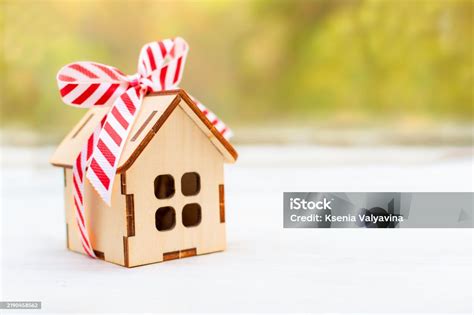 창문 근처의 테이블에 흰색 빨간색 포장 리본으로 만든 묶인 활이 있는 목조 주택의 모델 복사 공간이 있는 배경 선물 선물 새 집