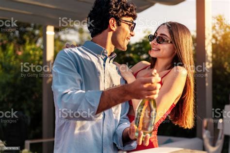 사랑하는 부부는 약혼 파티를 축하하기 위해 테이블에 앉아있는 친구 옆에 샴페인 한 병을 엽니 다 민박에 대한 스톡 사진 및 기타